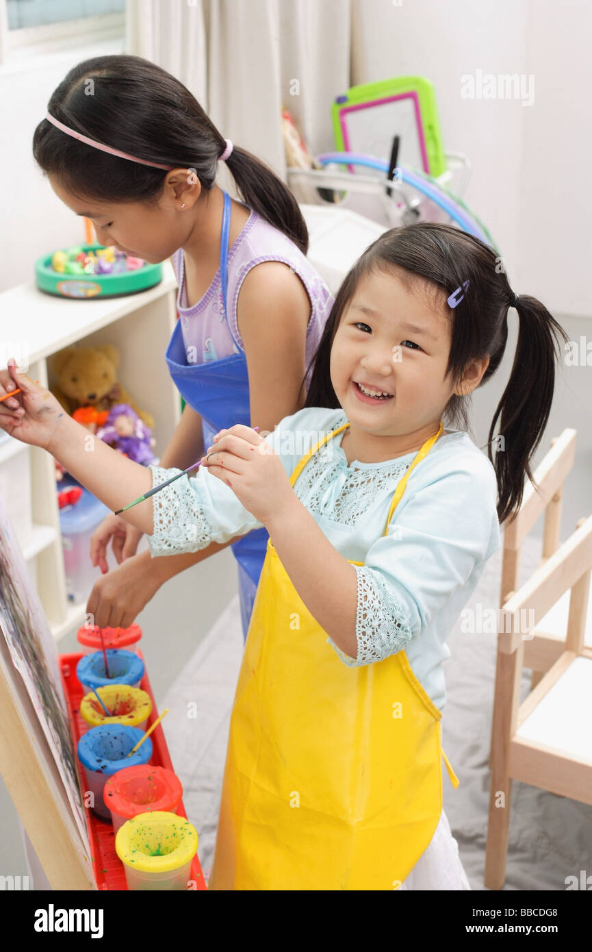 Two girls painting on easel, smiling Stock Photo - Alamy