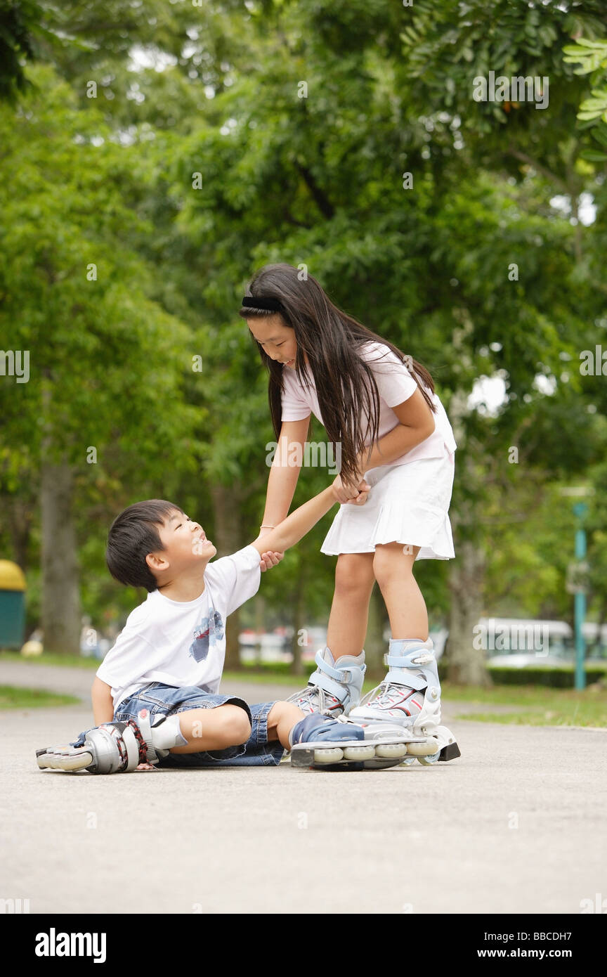 Children rollerblading, boy on the ground, girl pulling him up Stock ...