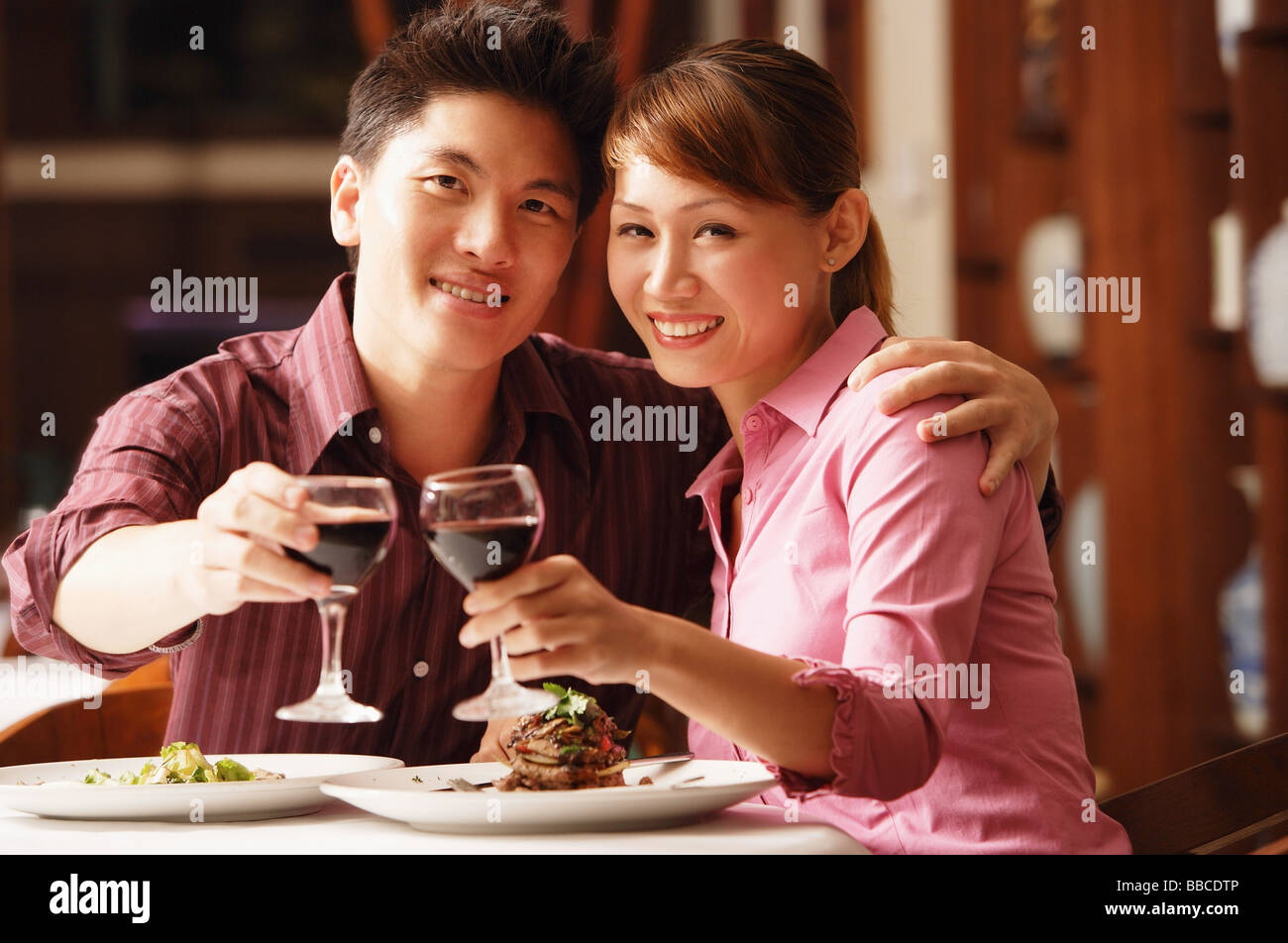 Couple in restaurant, looking at camera, toasting with wine glasses ...