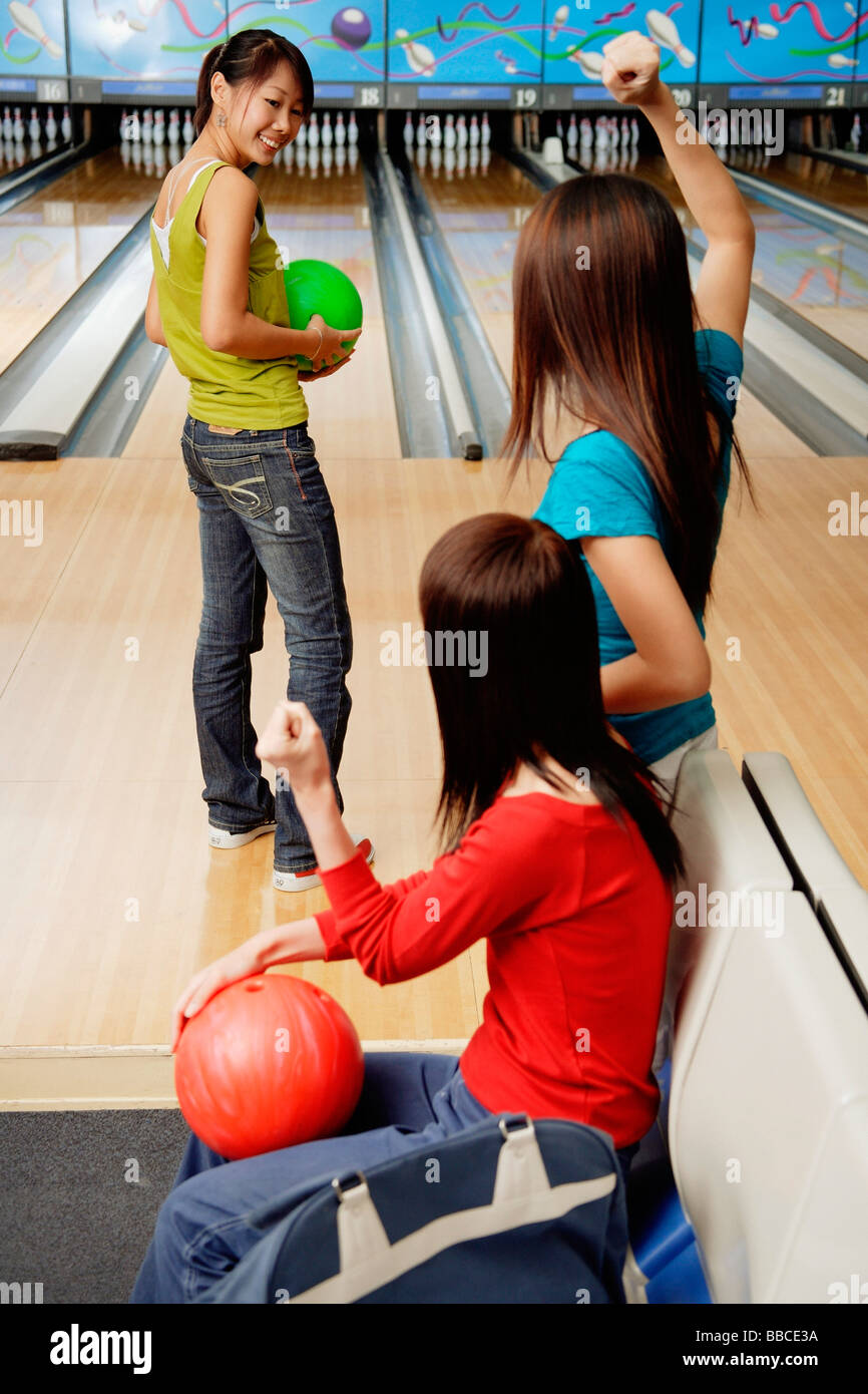 Women in bowling alley, one woman about to bowl, friends cheering her ...