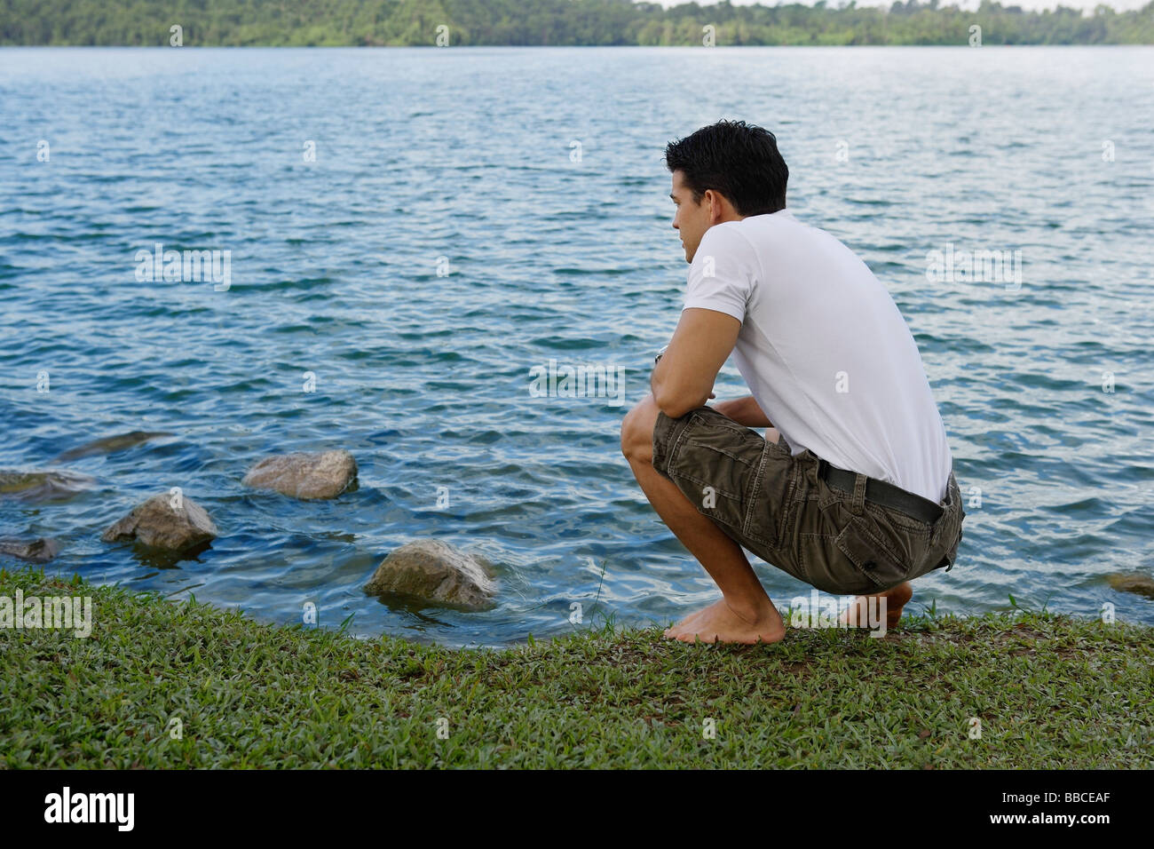 Man bending down next to lake Stock Photo - Alamy
