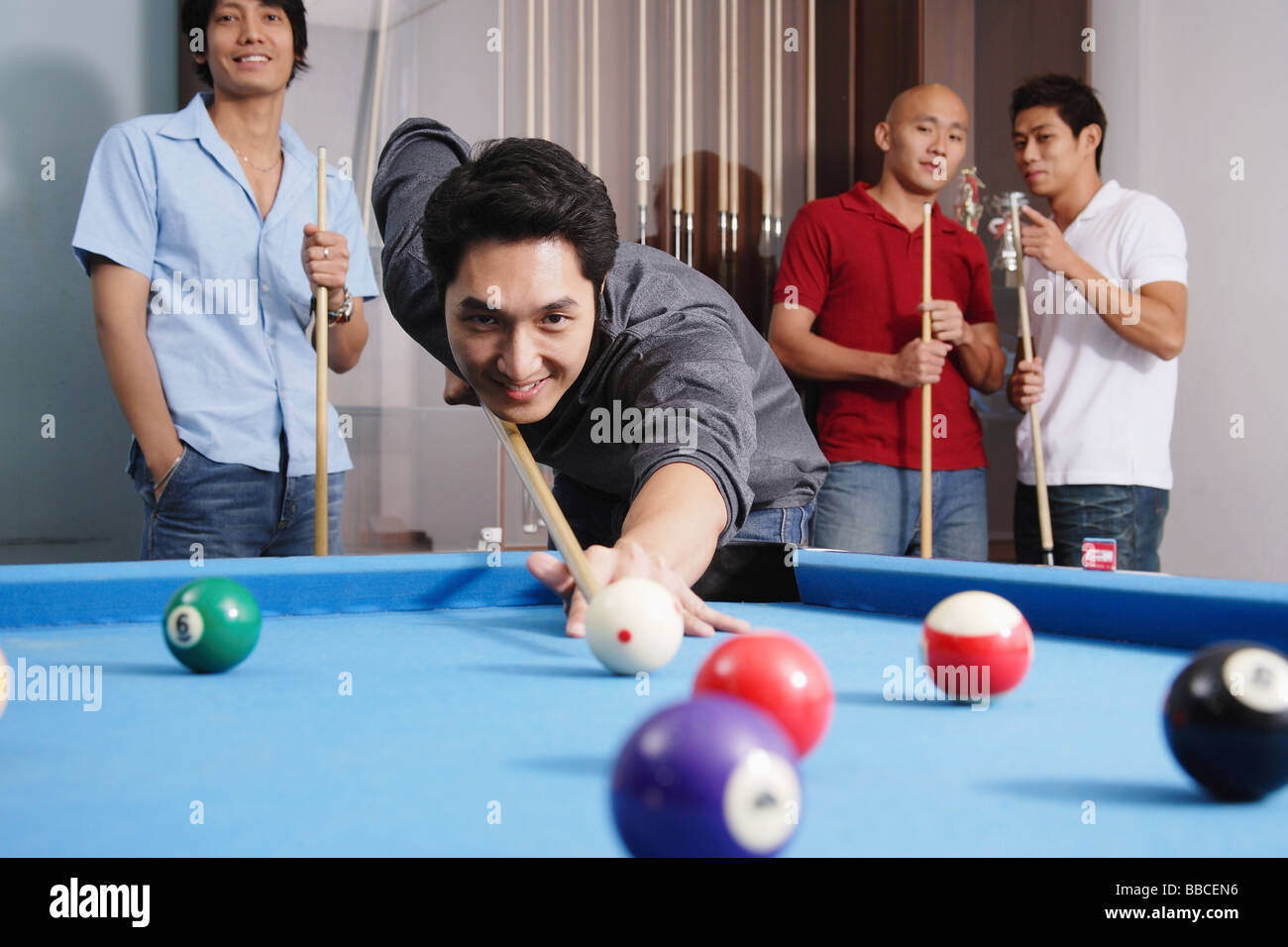 Man aiming pool cue at ball, other men watching in the background Stock ...