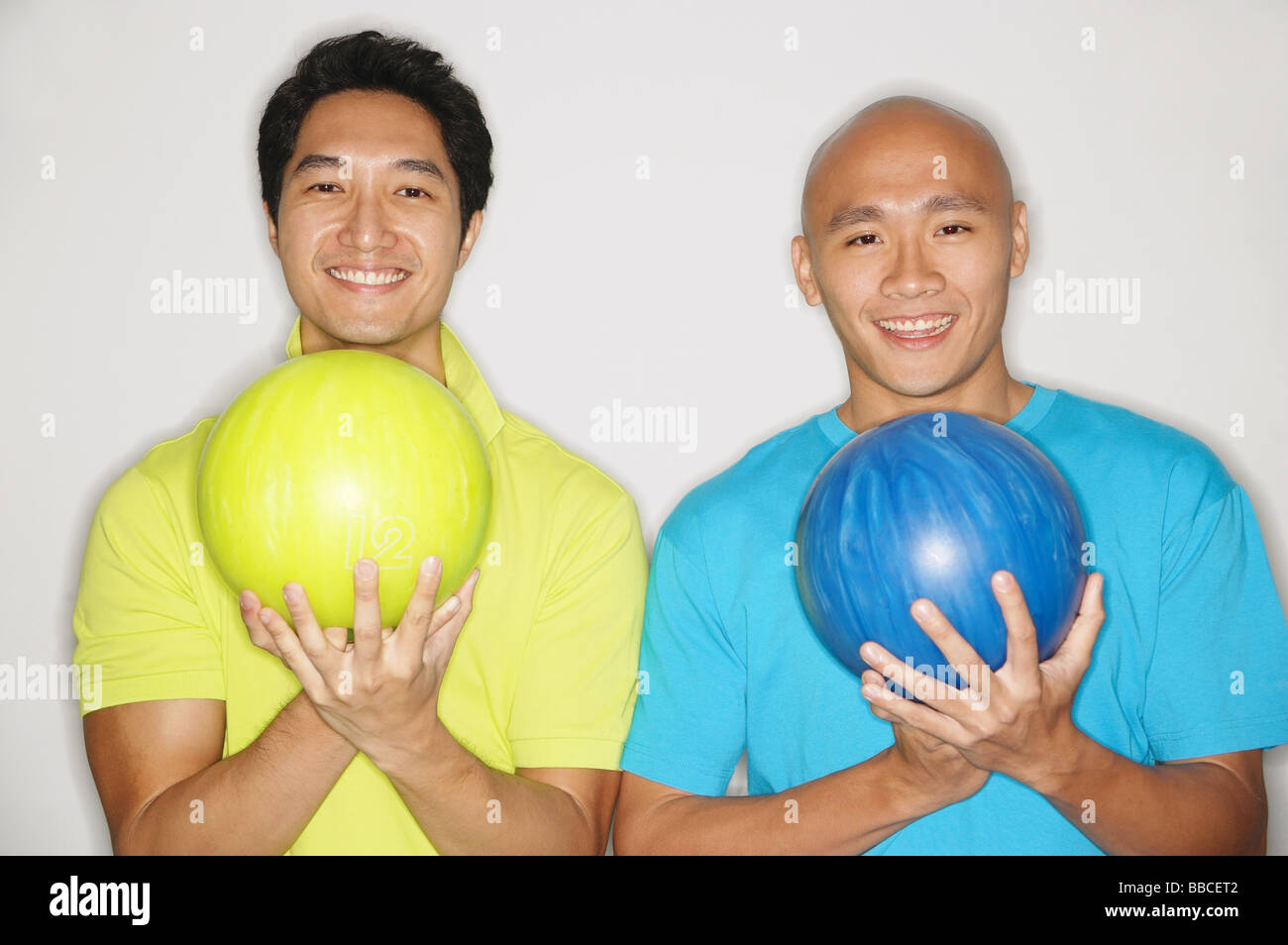 Two men standing side by side, carrying bowling balls, smiling at ...
