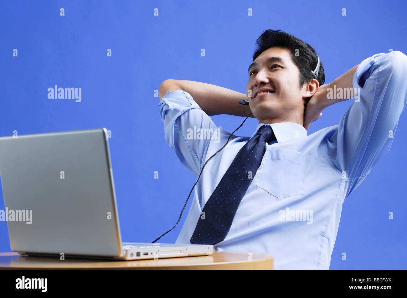 Man wearing headset, using laptop, leaning back, hands behind head ...
