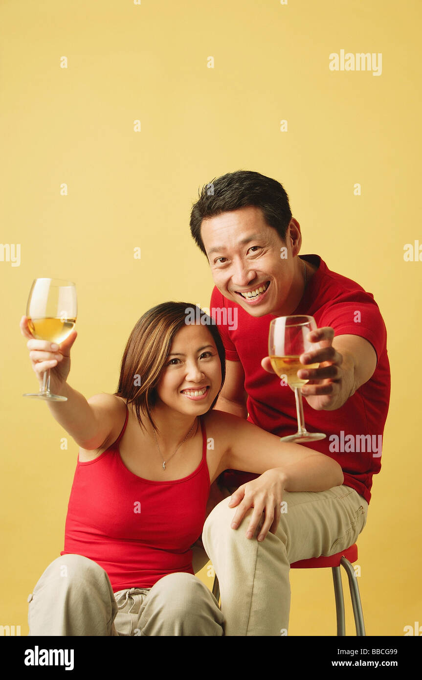 Couple sitting, raising drinks towards camera Stock Photo - Alamy