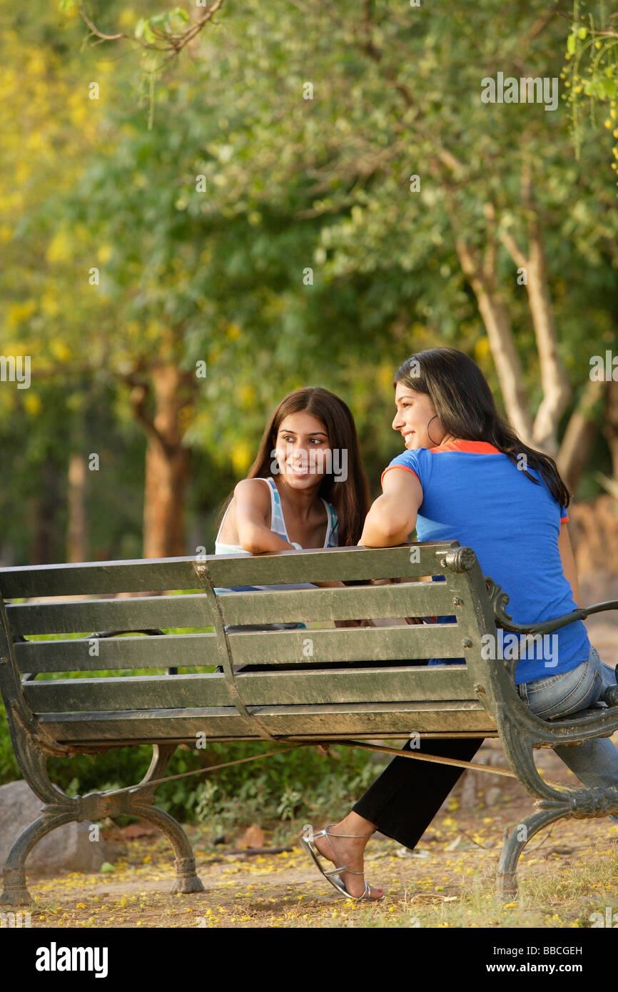 Two teen girls sitting on park bench Stock Photo - Alamy