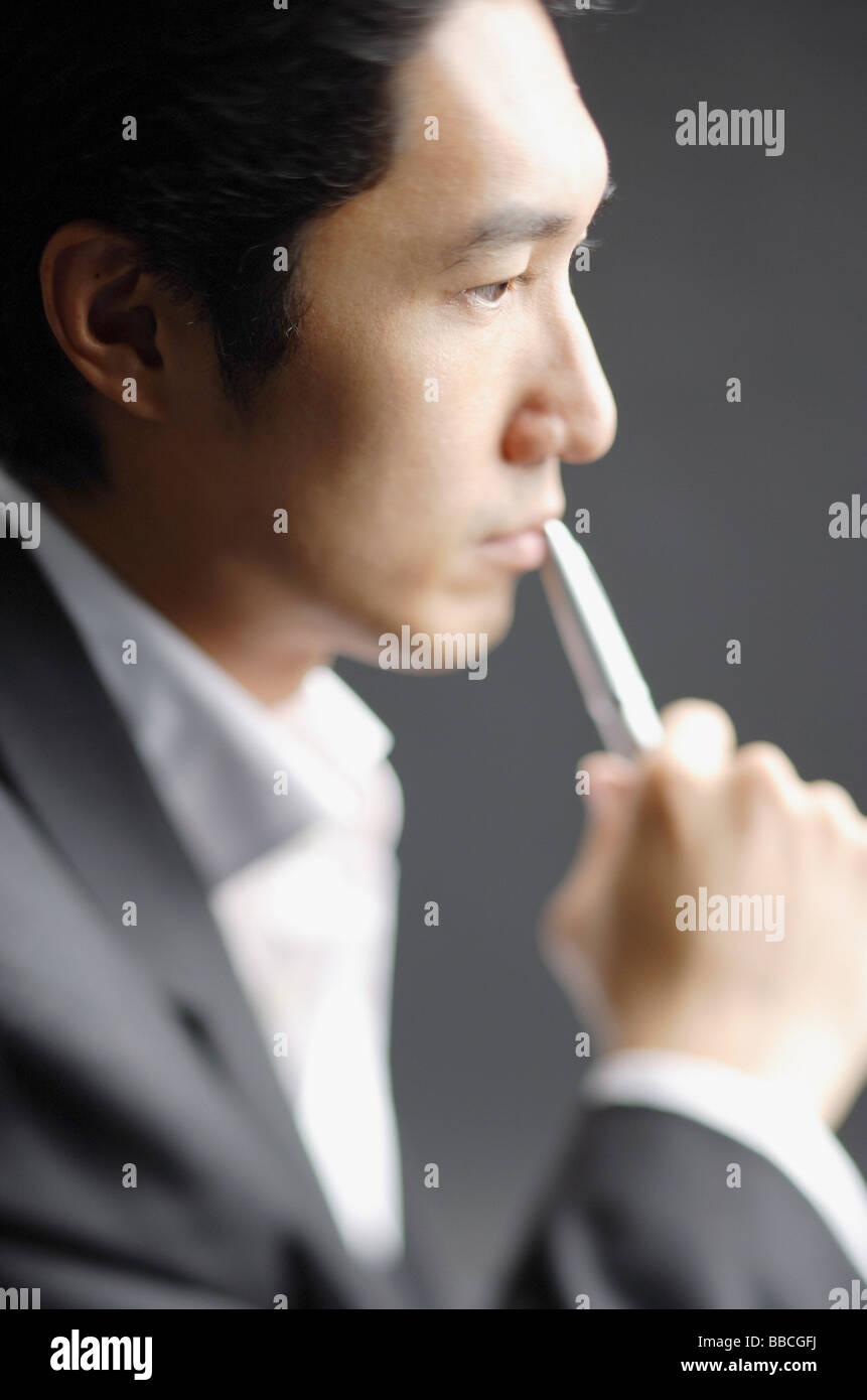 Man holding pen to mouth, side view Stock Photo - Alamy