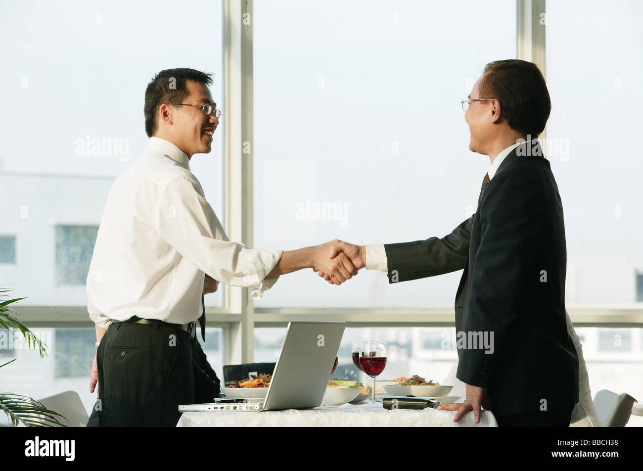 Businessmen shaking hands over lunch table Stock Photo - Alamy