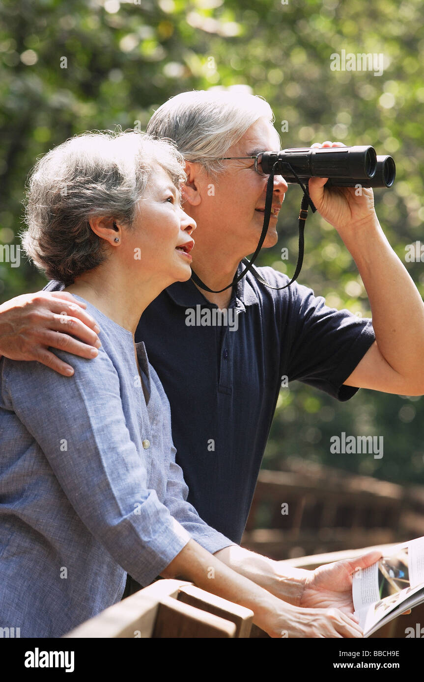 Senior couple side by side, man using binoculars Stock Photo - Alamy