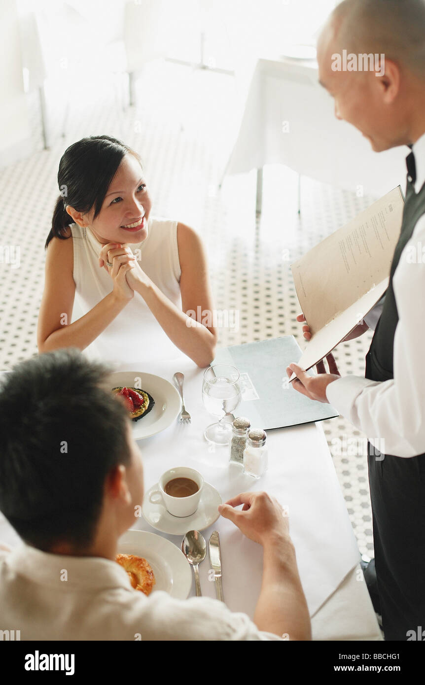 Waiter showing menu to couple at restaurant, woman smiling at him Stock ...