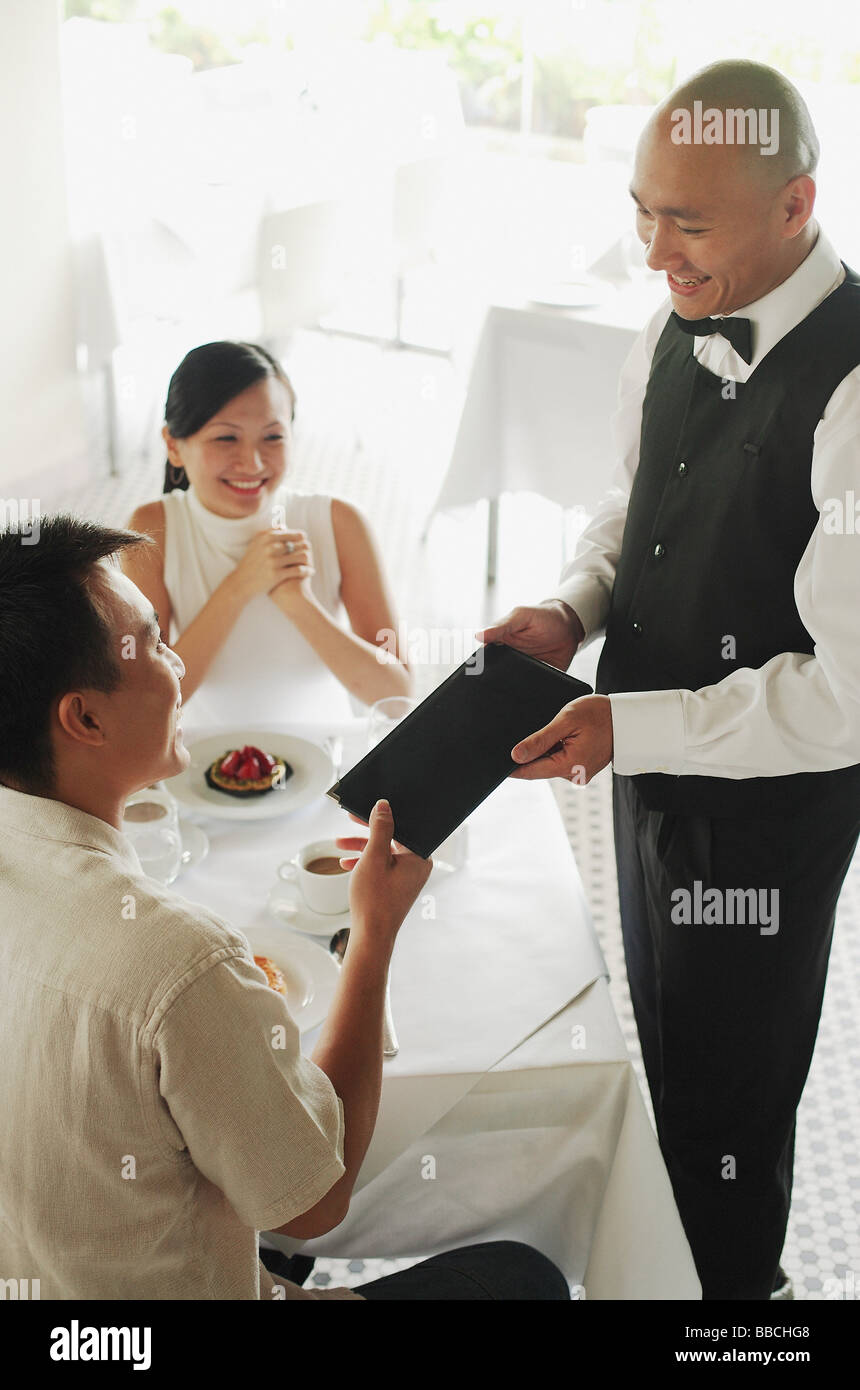 Couple in restaurant, man handing menu back to waiter Stock Photo - Alamy