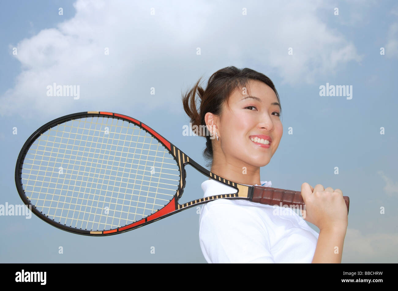 Young woman holding tennis racket over shoulder, smiling at camera ...