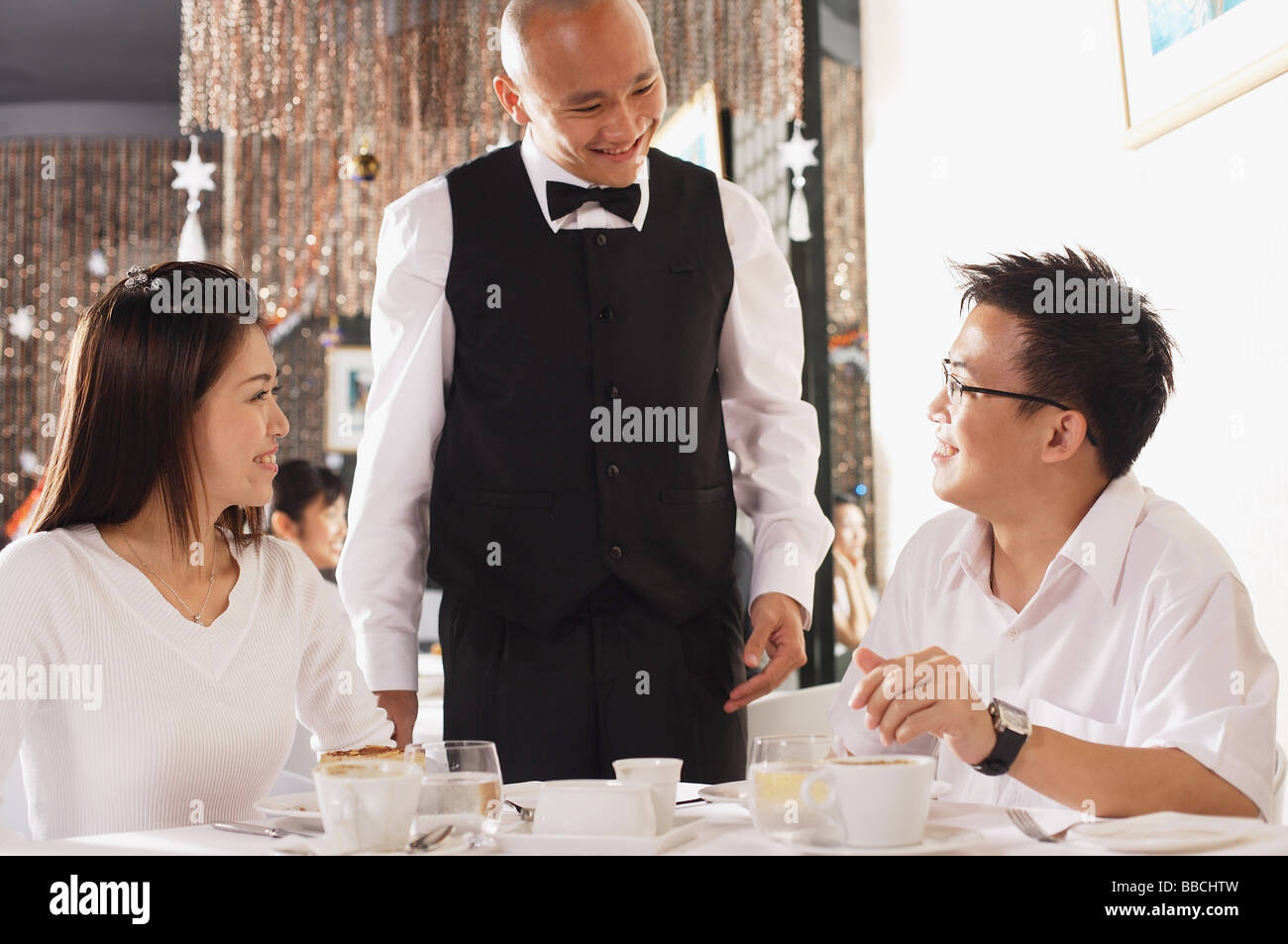 Couple in restaurant, waiter standing and smiling at them Stock Photo ...