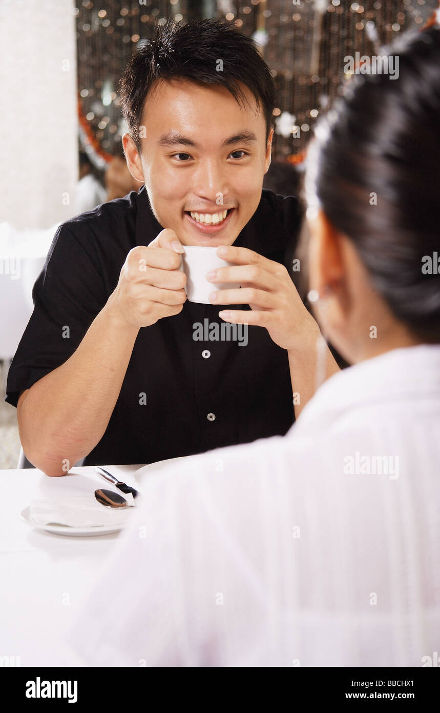 Couple eating in restaurant, man holding cup, over the shoulder view ...