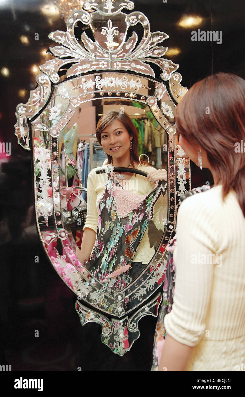 Woman in clothing store, holding dress, looking at mirror Stock Photo ...