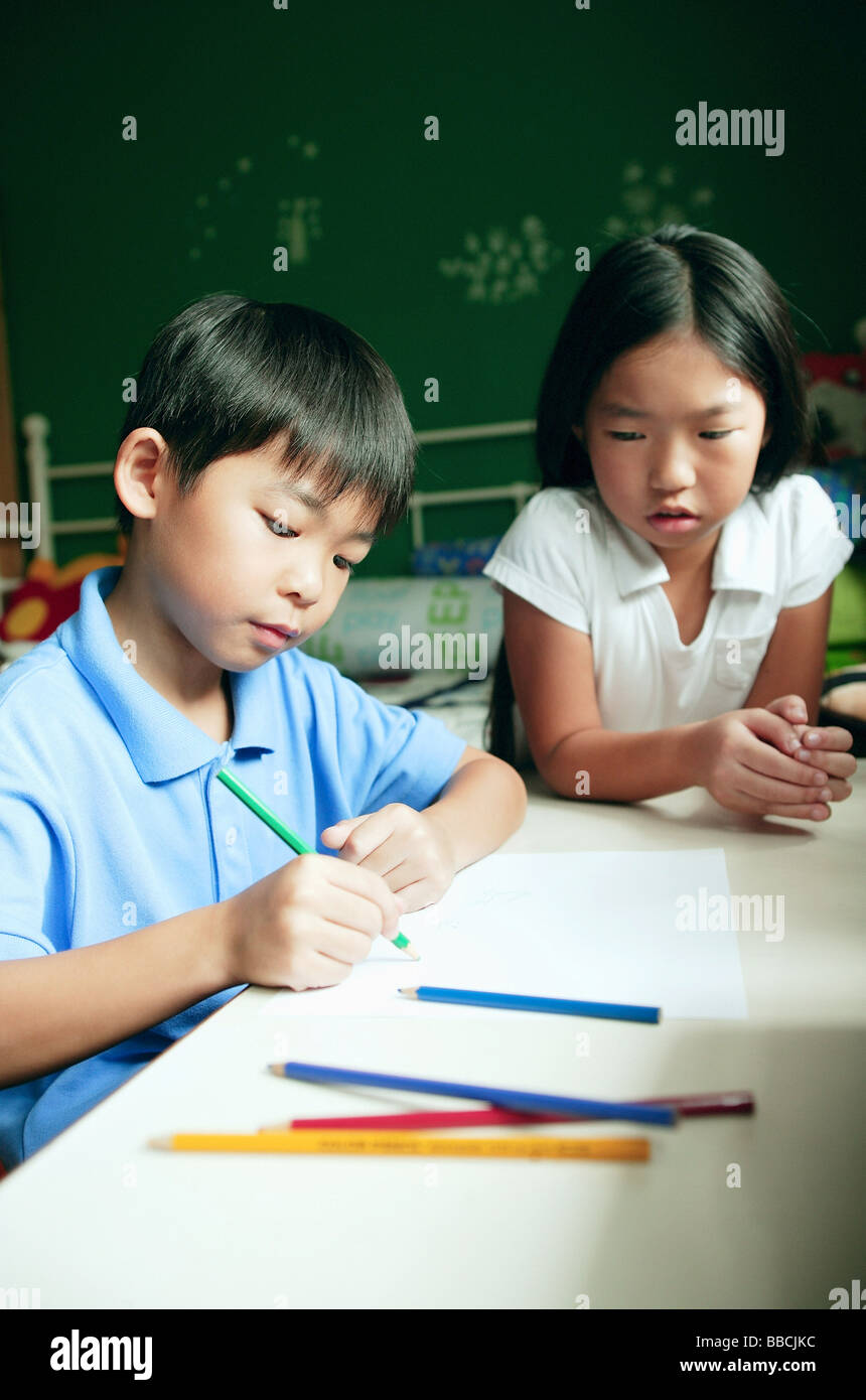 Boy in bedroom, drawing on paper, sister next to him watching Stock ...