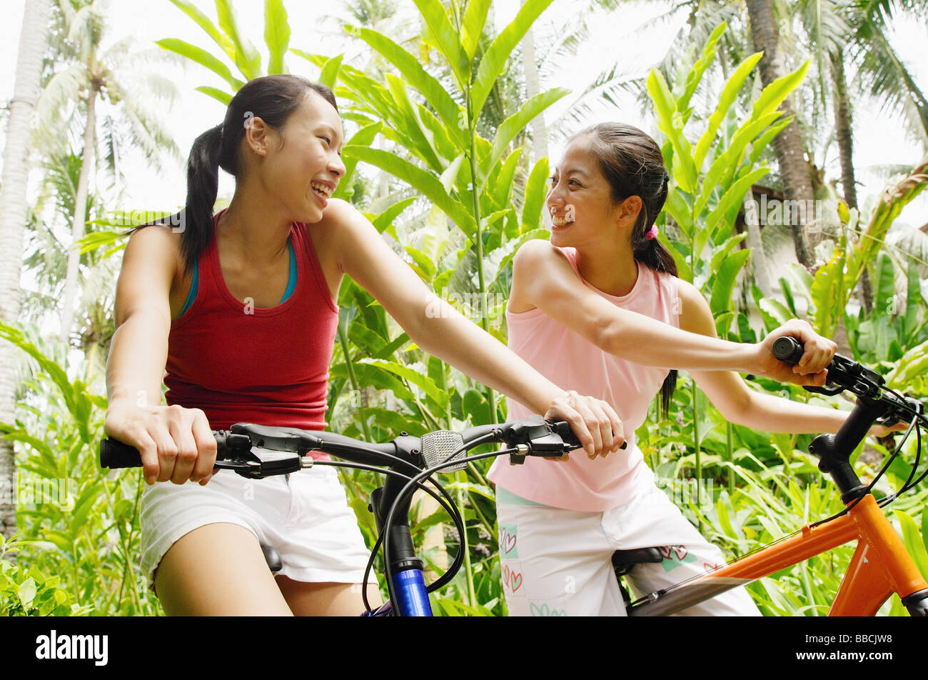Two girls riding bikes through a park, looking at each other Stock ...