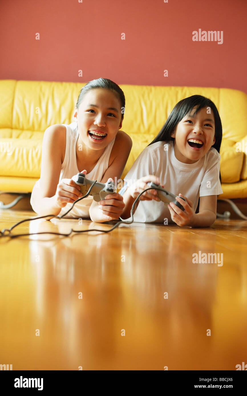 Two sisters lying on floor playing video games, smiling Stock Photo - Alamy
