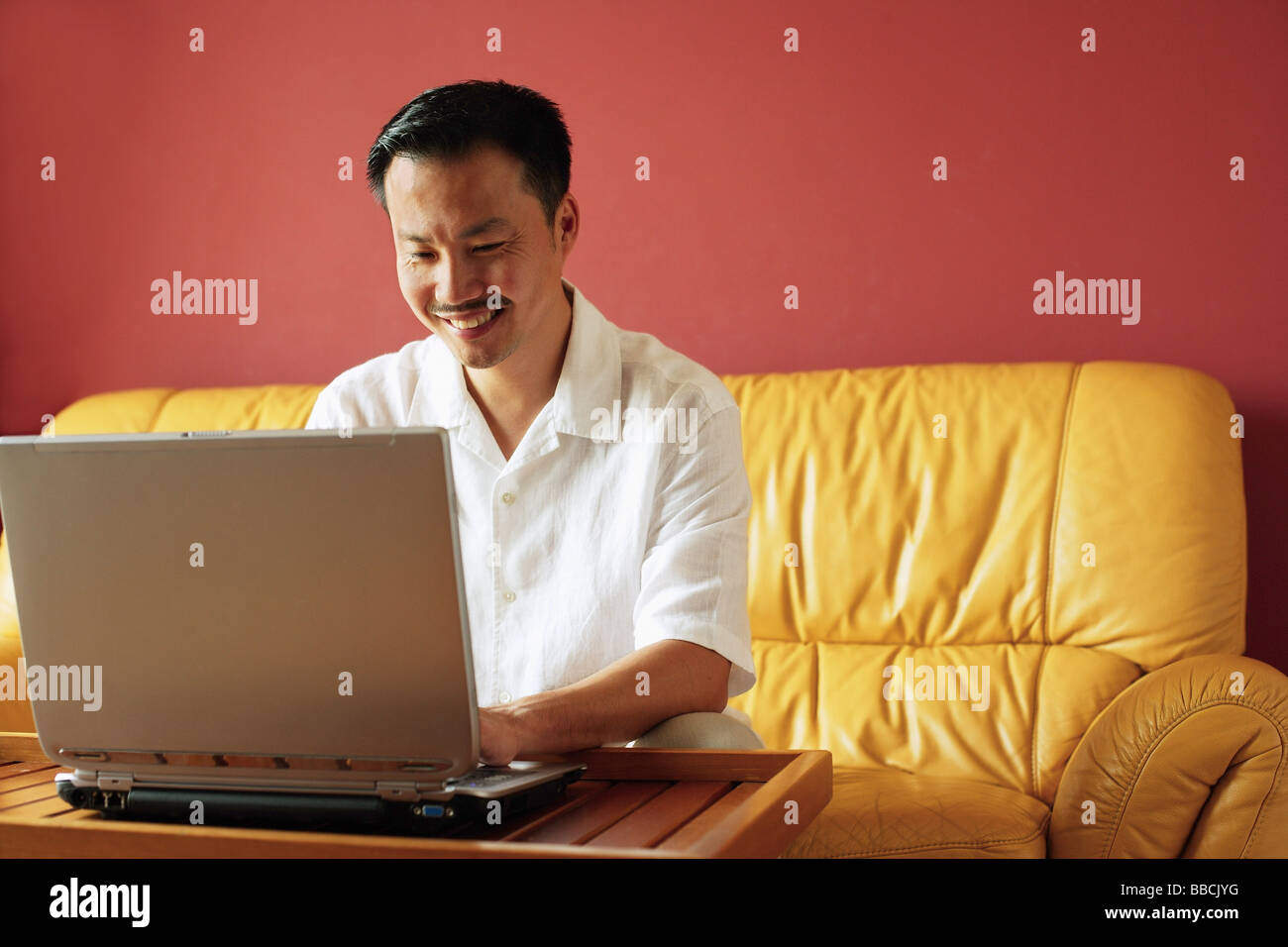 Man sitting on sofa, using laptop Stock Photo - Alamy