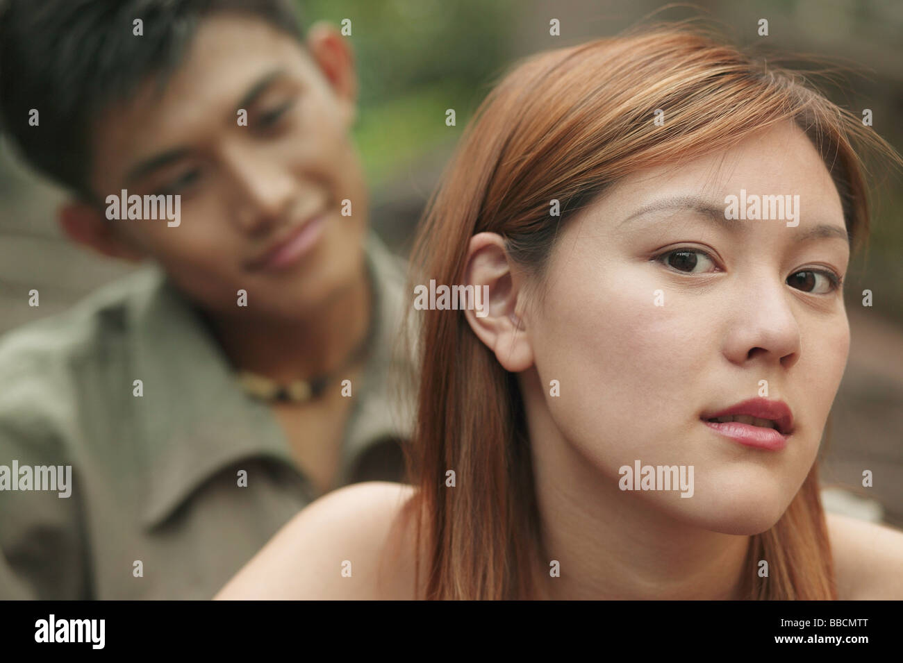 Young woman looking at camera, young man in the background Stock Photo ...