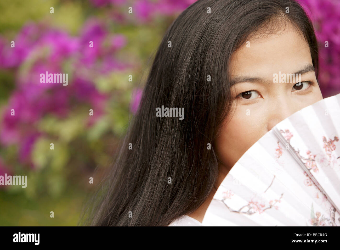 Young woman peeking over fan Stock Photo - Alamy