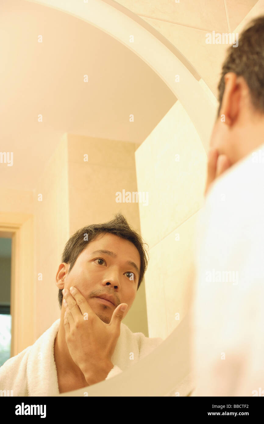 Young man touching his face, looking in mirror Stock Photo - Alamy