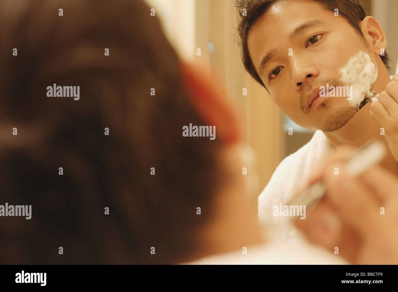 Young man shaving, looking in mirror, over the shoulder view Stock ...