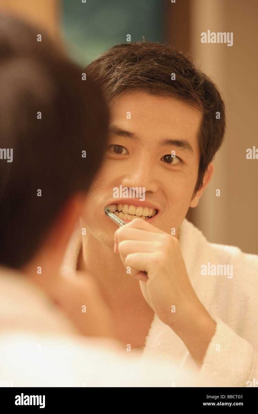 Young man brushing his teeth, looking in mirror Stock Photo - Alamy