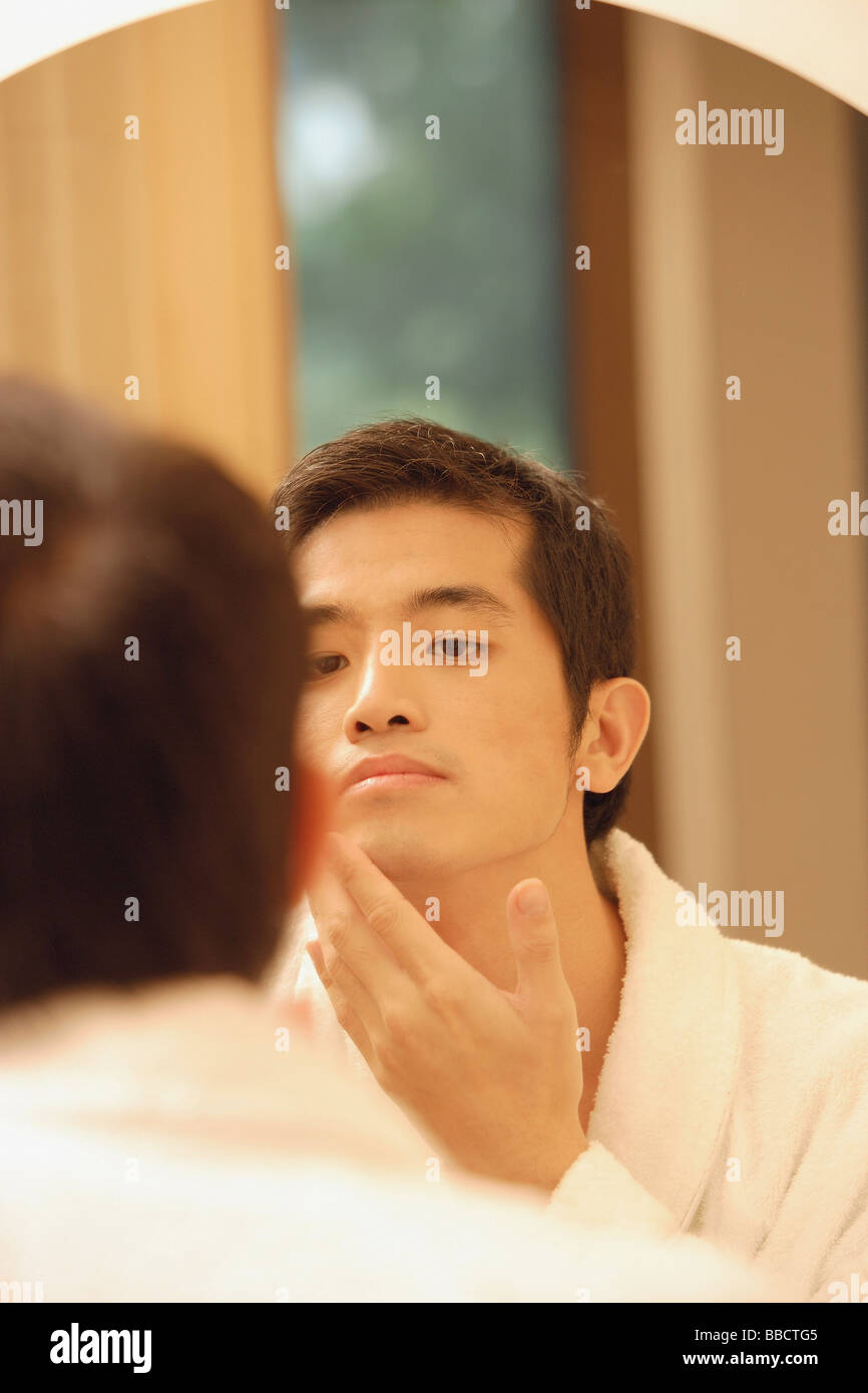 Young man looking in mirror, touching his face Stock Photo - Alamy