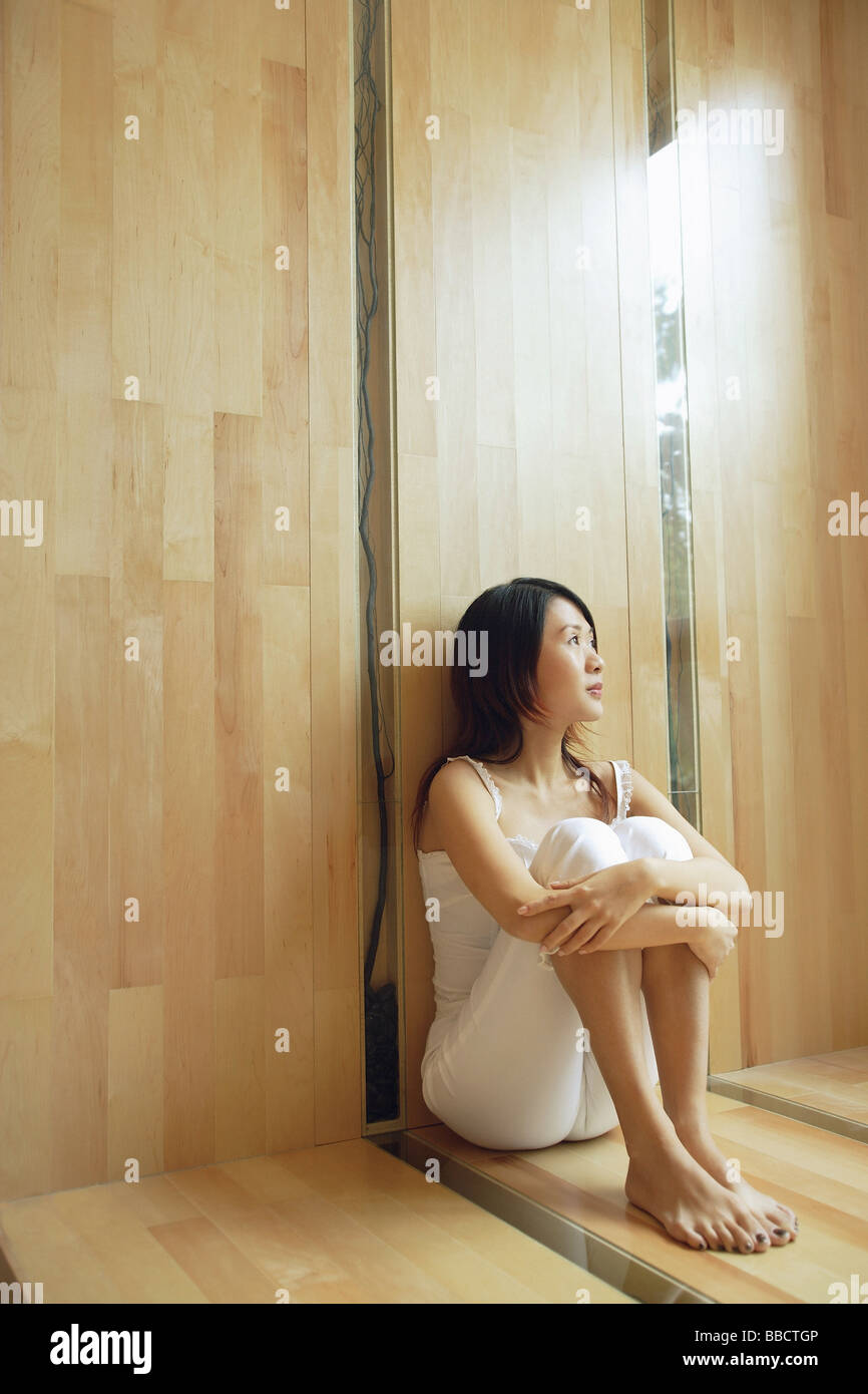 Young woman sitting, hugging knees, looking up Stock Photo - Alamy
