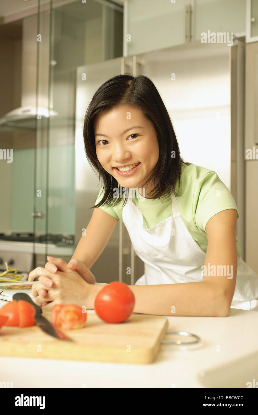 Young woman leaning on kitchen counter, hands clasped, looking at ...
