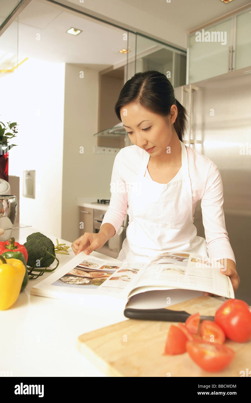 Young woman standing at kitchen counter, looking at cookbook Stock ...