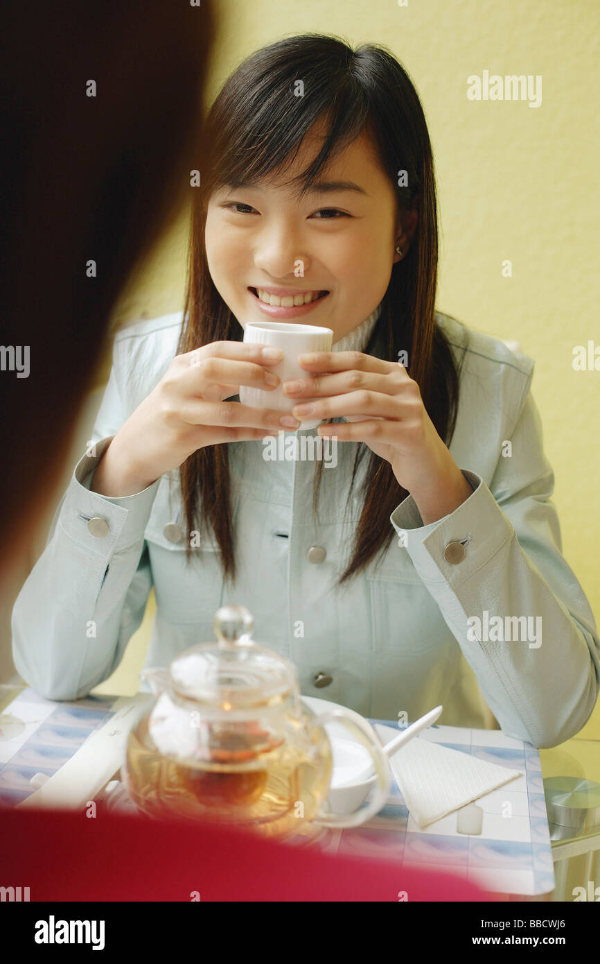Young woman drinking tea, facing another person Stock Photo - Alamy