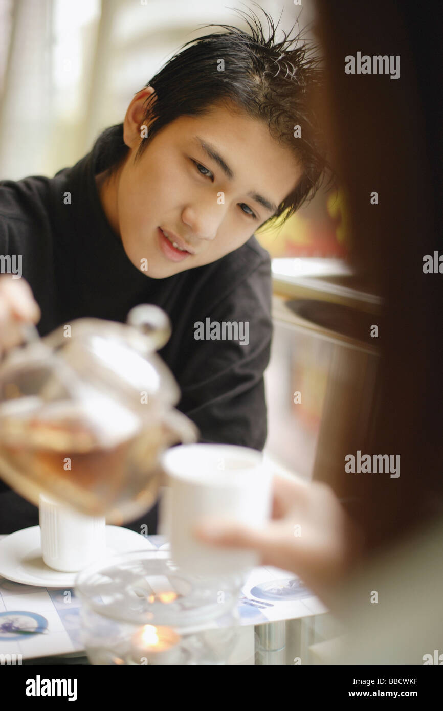 Young man pouring tea for young woman in front of him Stock Photo - Alamy