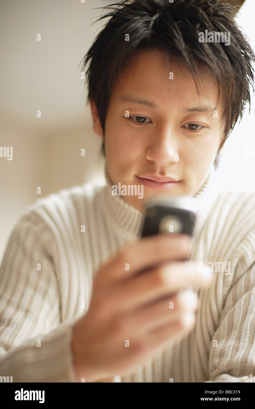 Young man holding mobile phone, looking down Stock Photo - Alamy