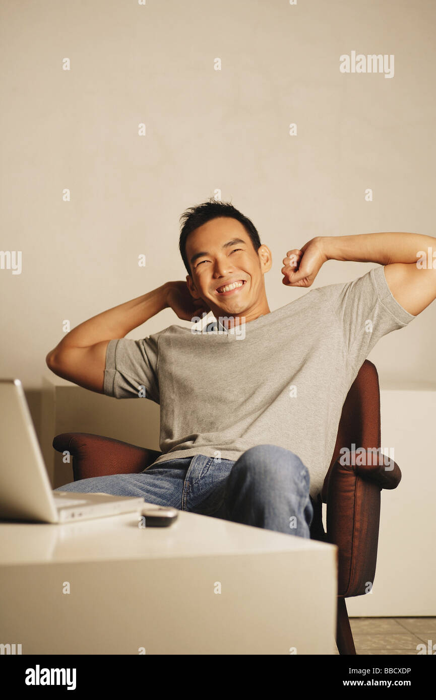 Man stretching while sitting on chair, laptop open in front of him ...