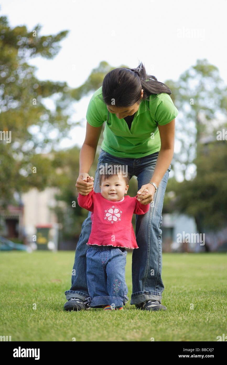 Baby girl standing, mother guiding her Stock Photo - Alamy