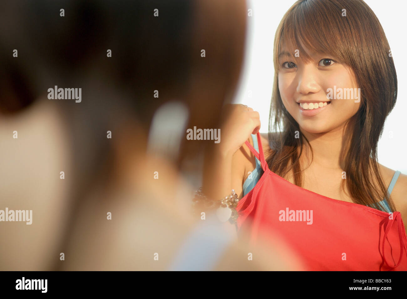 Young woman looking at mirror, holding up tank top Stock Photo - Alamy