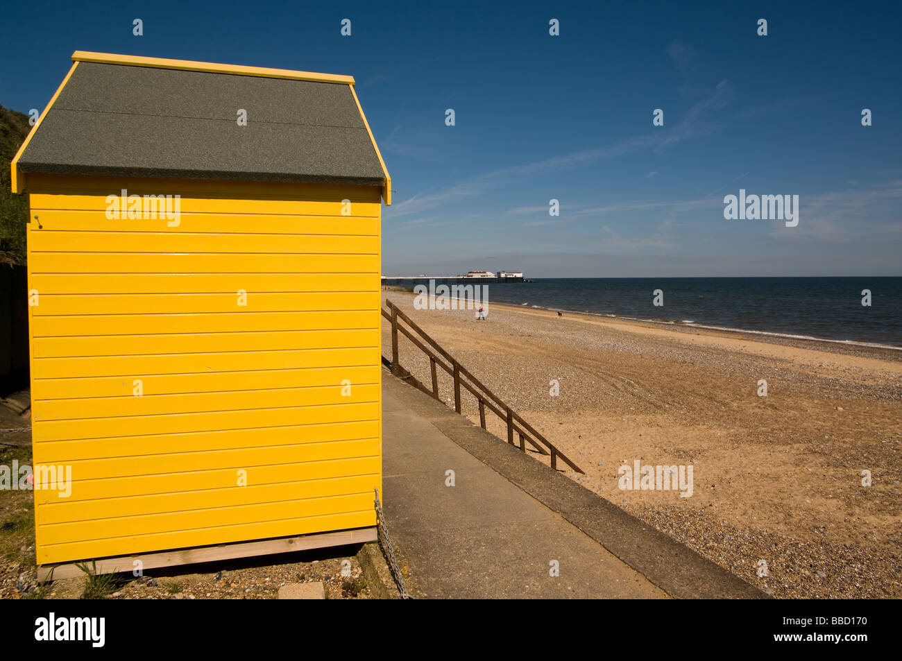 A yellow beach hut on Cromer sea front with the pier in the far ...