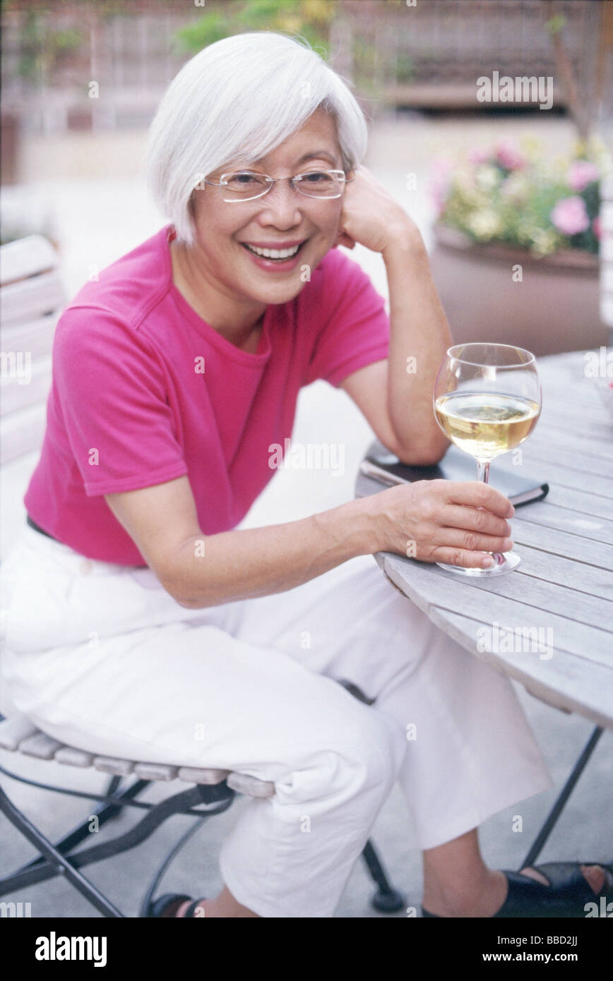 Mature woman sitting outdoors with wine glass, looking at camera Stock ...