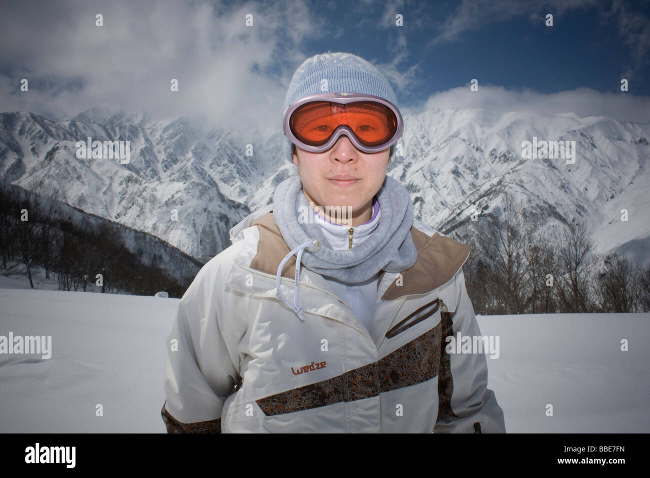 A female snowboarder with orange goggles stands in front of majestic ...