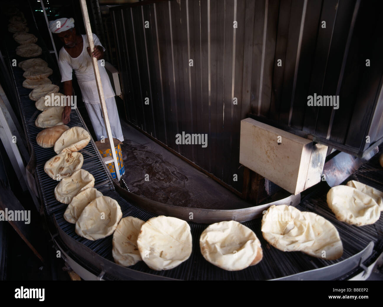 QATAR Doha Single man beside conveyor in bakery as round Arab bread ...