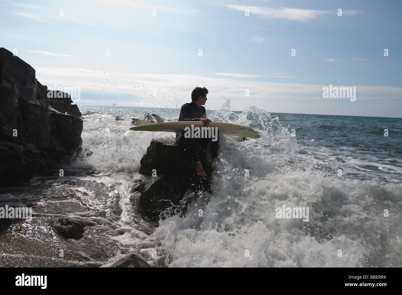 Young adult sitting on rock holding his surfboard Stock Photo - Alamy