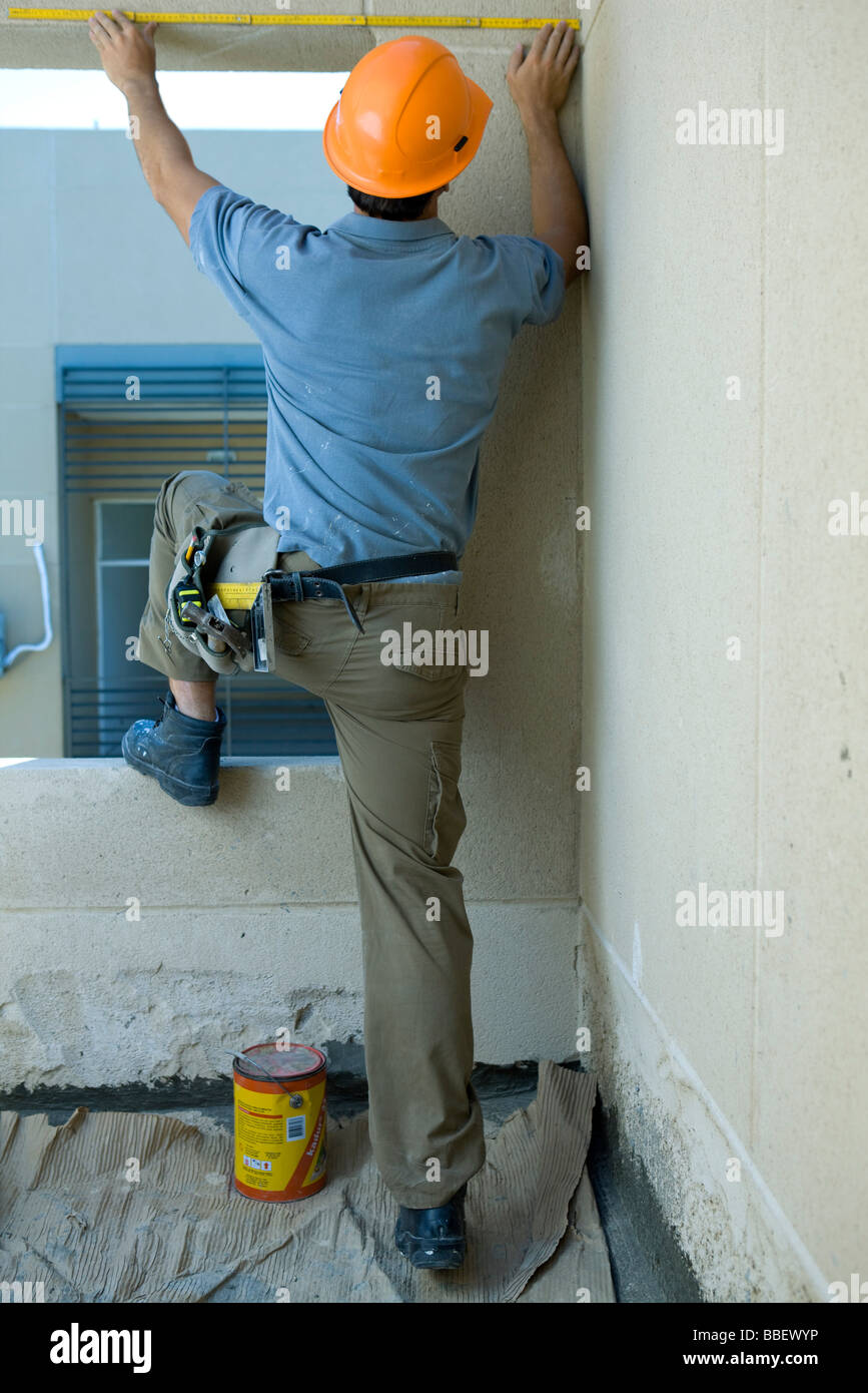 Construction worker with foot on windowsill measuring space above ...