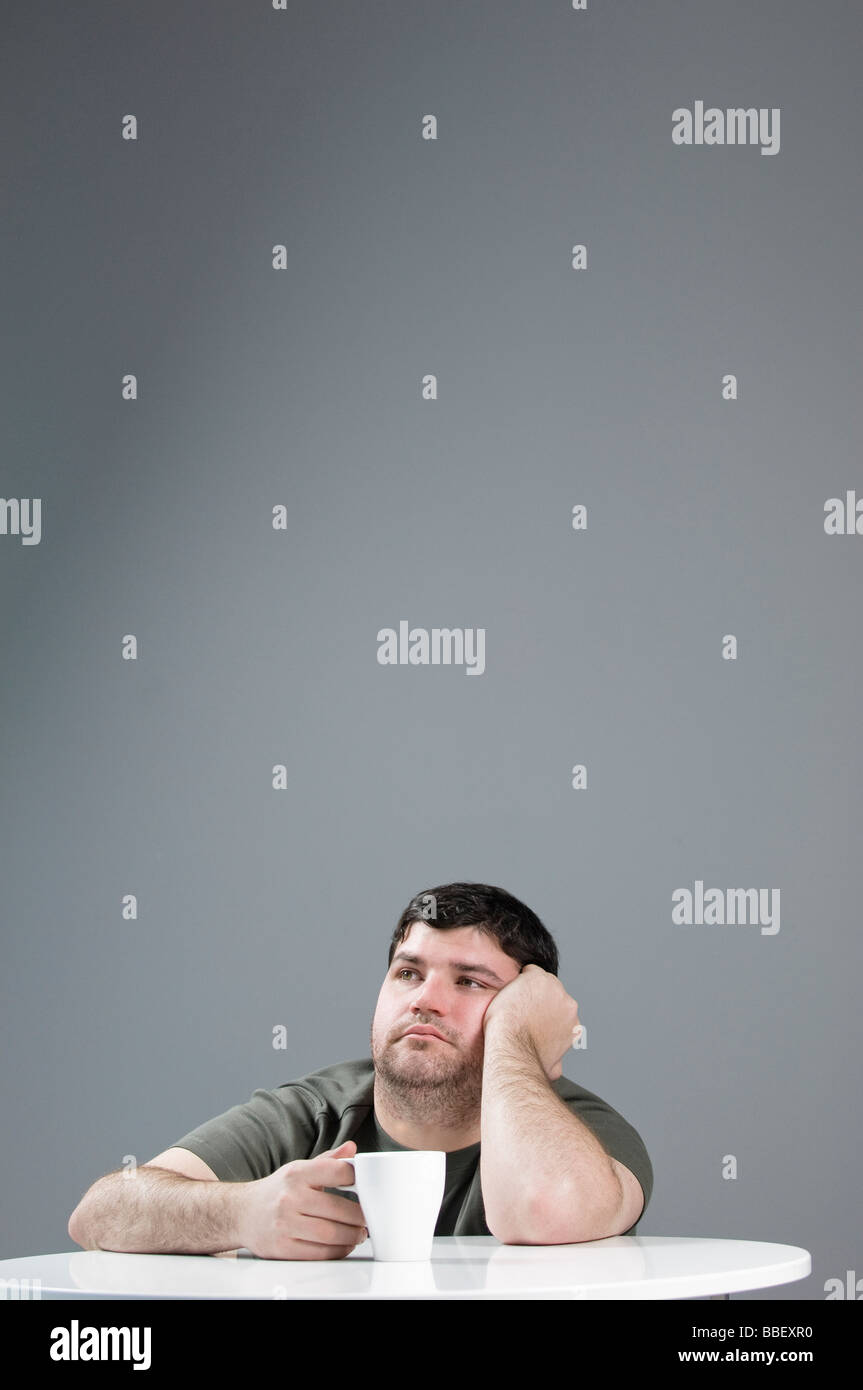 Man looking sad with a coffee at a table on a grey background Stock ...