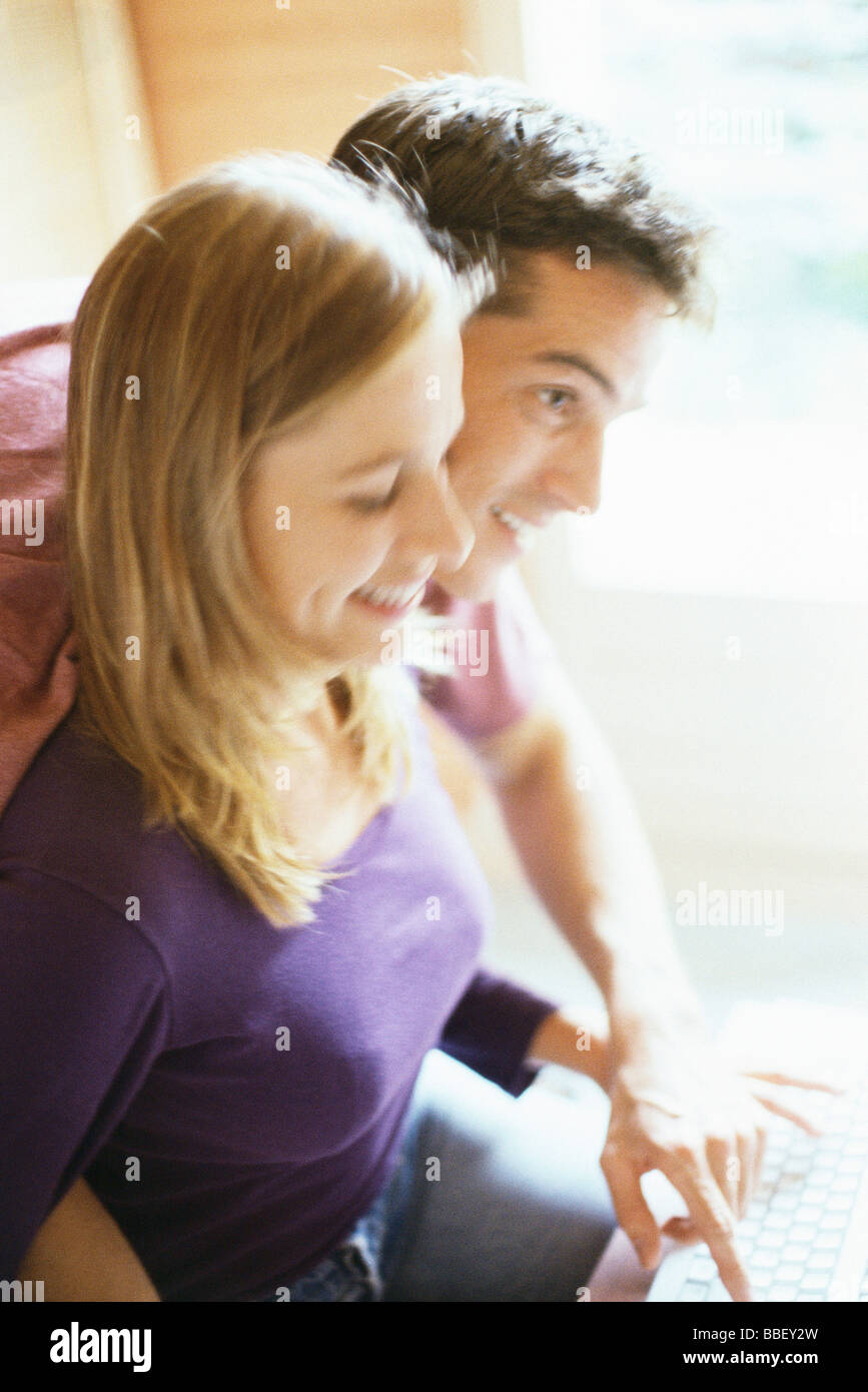 Couple typing on keyboard together, man leaning over woman's shoulder ...