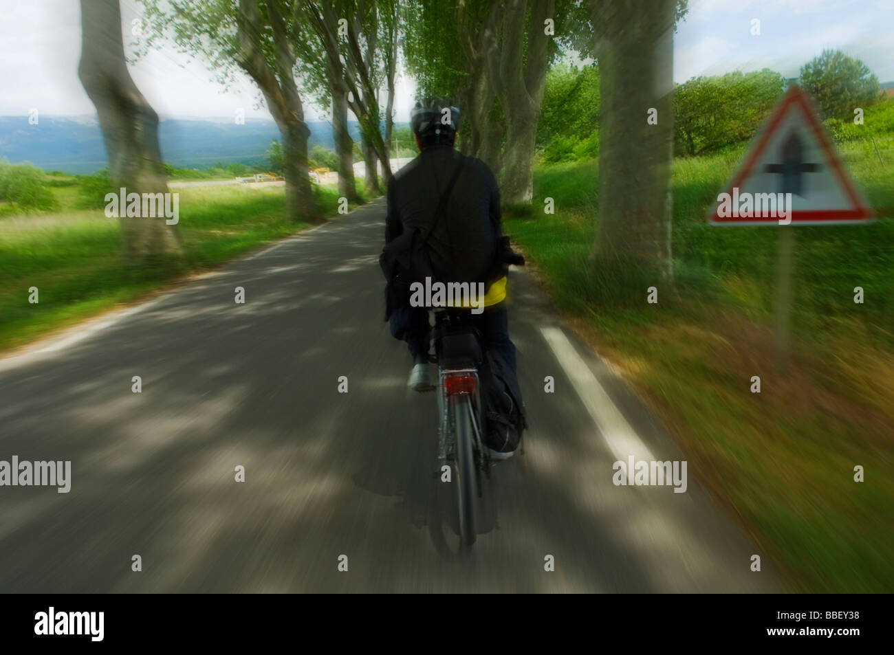 Rear view of an electric bike rider cycling along a tree lined road ...