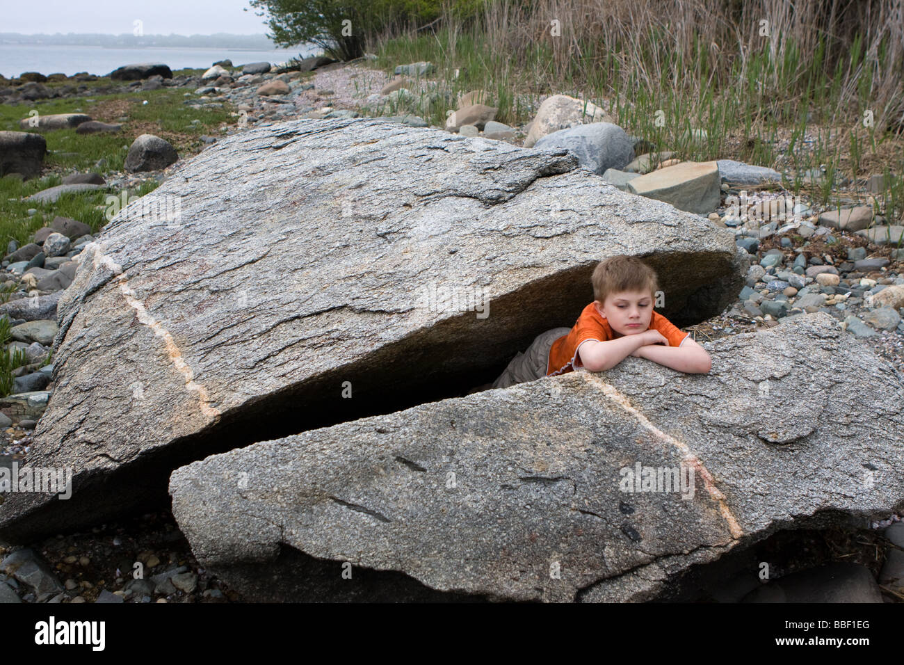 A small boy plays inside a massive cracked boulder along the shore in ...