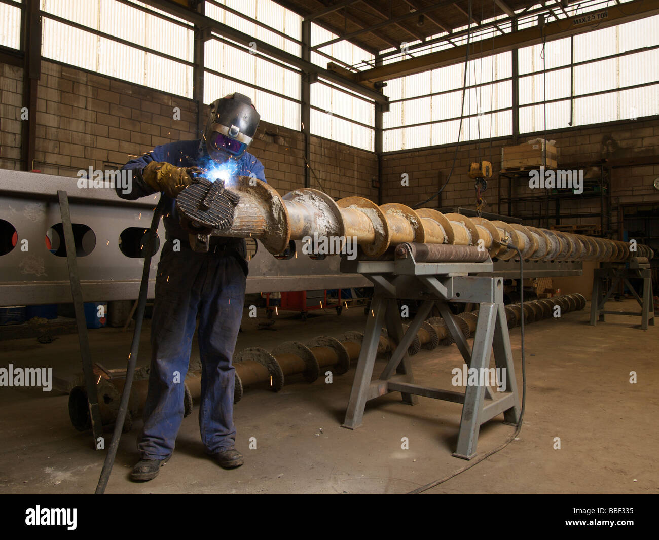 Man welding while refurbishing giant drill head inside industrial hall ...