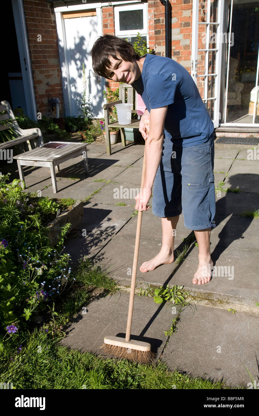 Teenage boy brushing patio with broom Stock Photo - Alamy